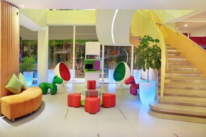 Espaço moderno em ambiente interno, com escada curva, áreas de estar coloridas e plantas.