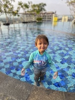 Uma criança parada na beira de uma piscina com chão de mosaico azul e verde.