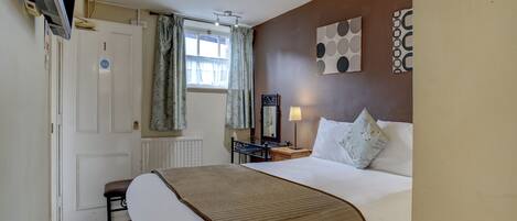 Quarto de hotel com cama, escrivaninha, cadeira, TV fixada na parede e janela com cortinas.