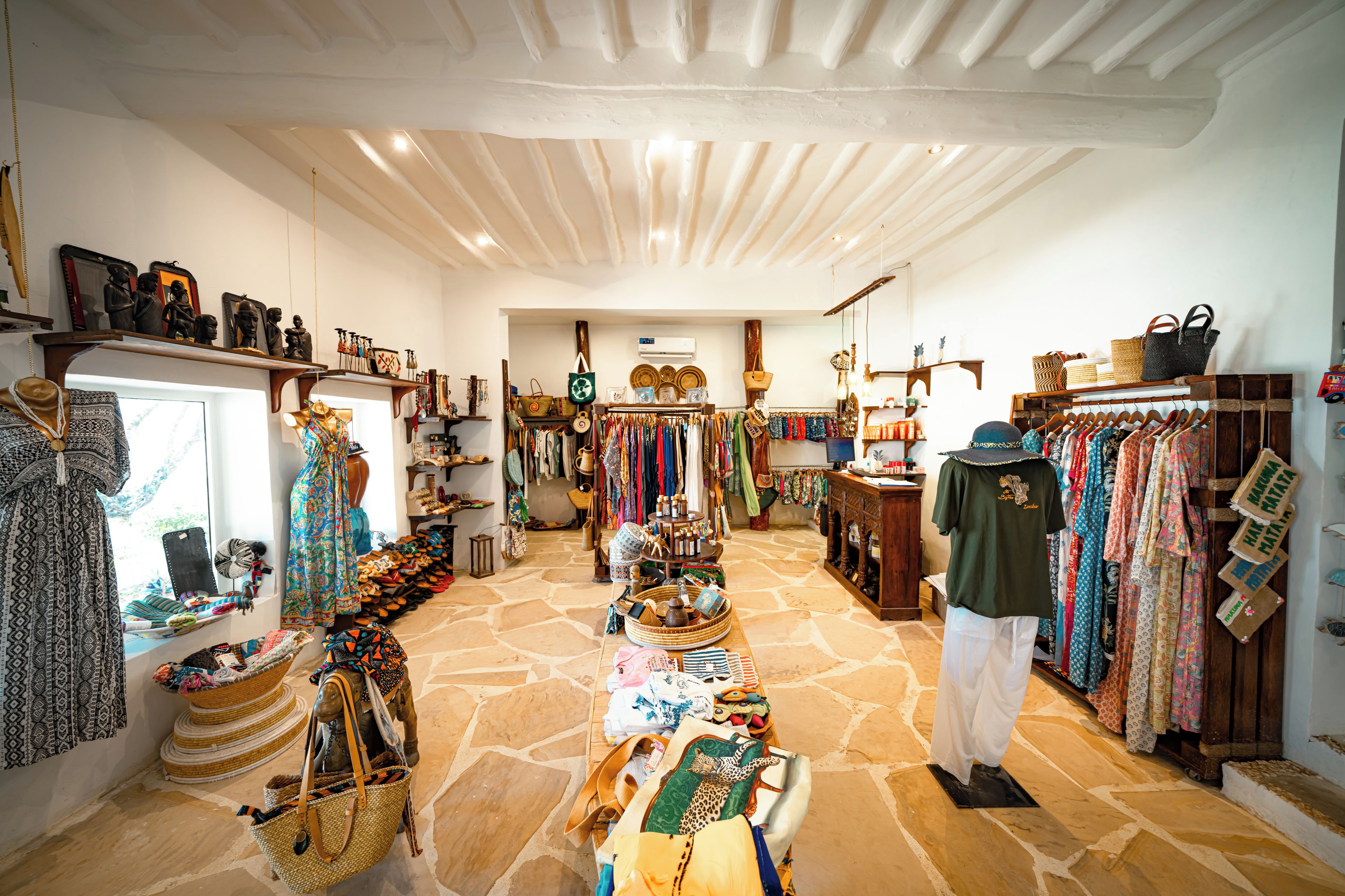 Uma loja boutique com diversas peças de roupa e acessórios expostos, incluindo vestidos estampados, bolsas e chapéus.