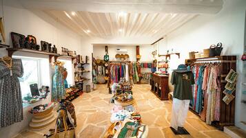 Uma loja boutique com diversas peças de roupa e acessórios expostos, incluindo vestidos estampados, bolsas e chapéus.
