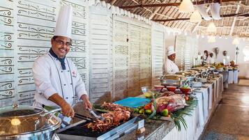 Disposição de buffet com um chefe preparando comida, variedade de pratos e uma parede decorativa com padrões.