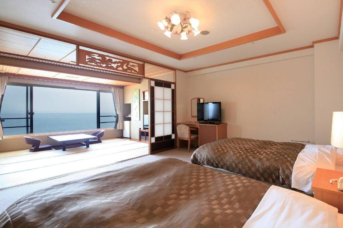 Quarto de hotel com cama, escrivaninha, televisão e vista para o mar.