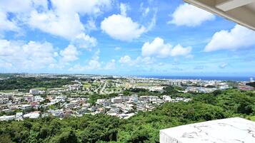 Vista panorâmica de uma cidade costeira com áreas residenciais densas, mistura de arquitetura moderna e tradicional, e céu azul límpido com nuvens dispersas.