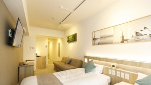 Quarto de hotel com duas camas, uma escrivaninha, um sofá e uma grande imagem emoldurada de uma vista urbana.