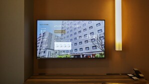 Televisão presa na parede exibindo um edifício com várias janelas e varandas.
