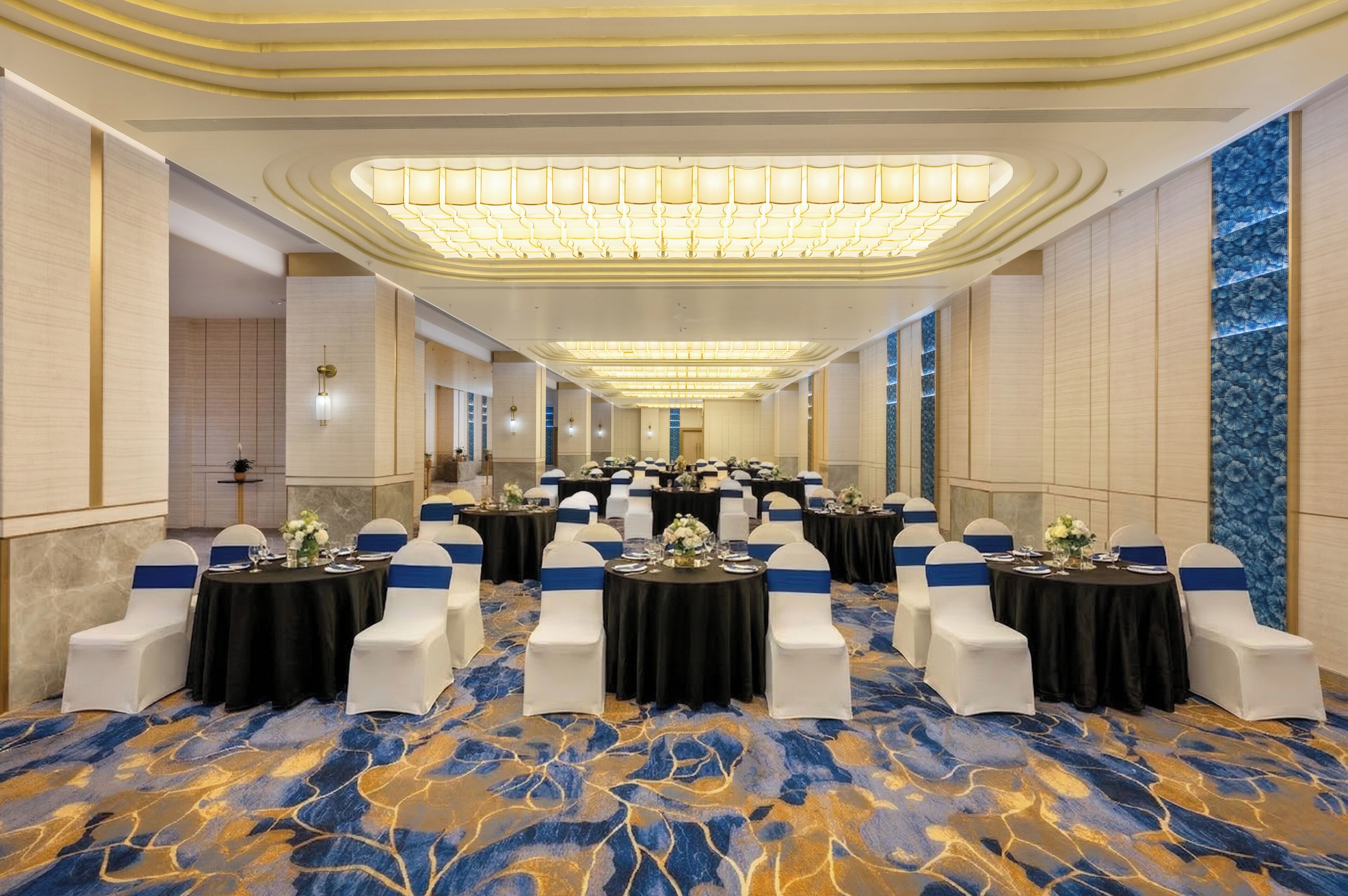 Uma sala de banquetes com mesas redondas, cadeiras brancas e um tapete azul.