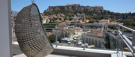 Varanda com cadeira suspensa, vista de uma cidade histórica com castelo no topo de uma colina e céu claro.