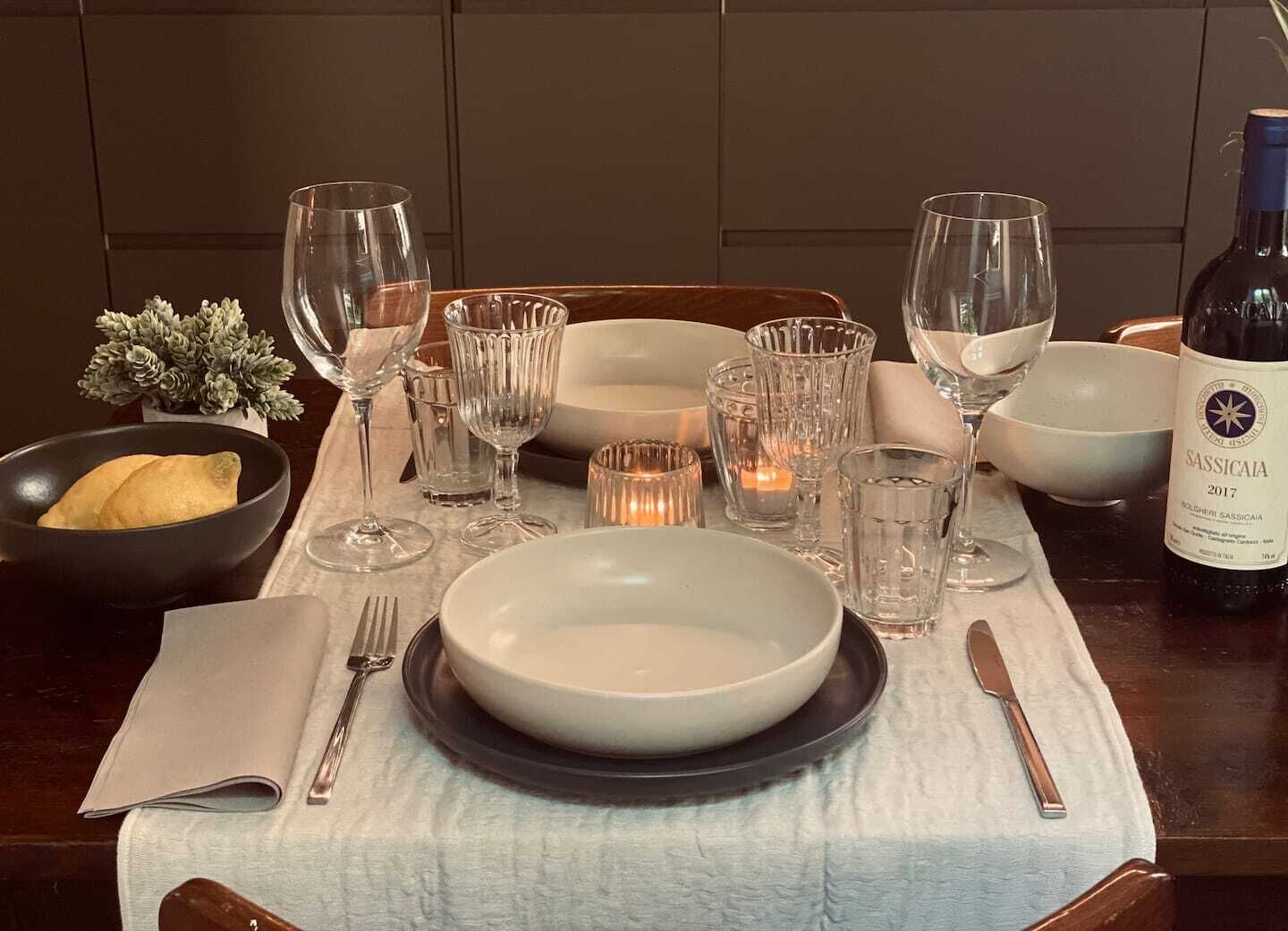 Mesa de jantar posta com pratos, copos, garrafa e velas.
