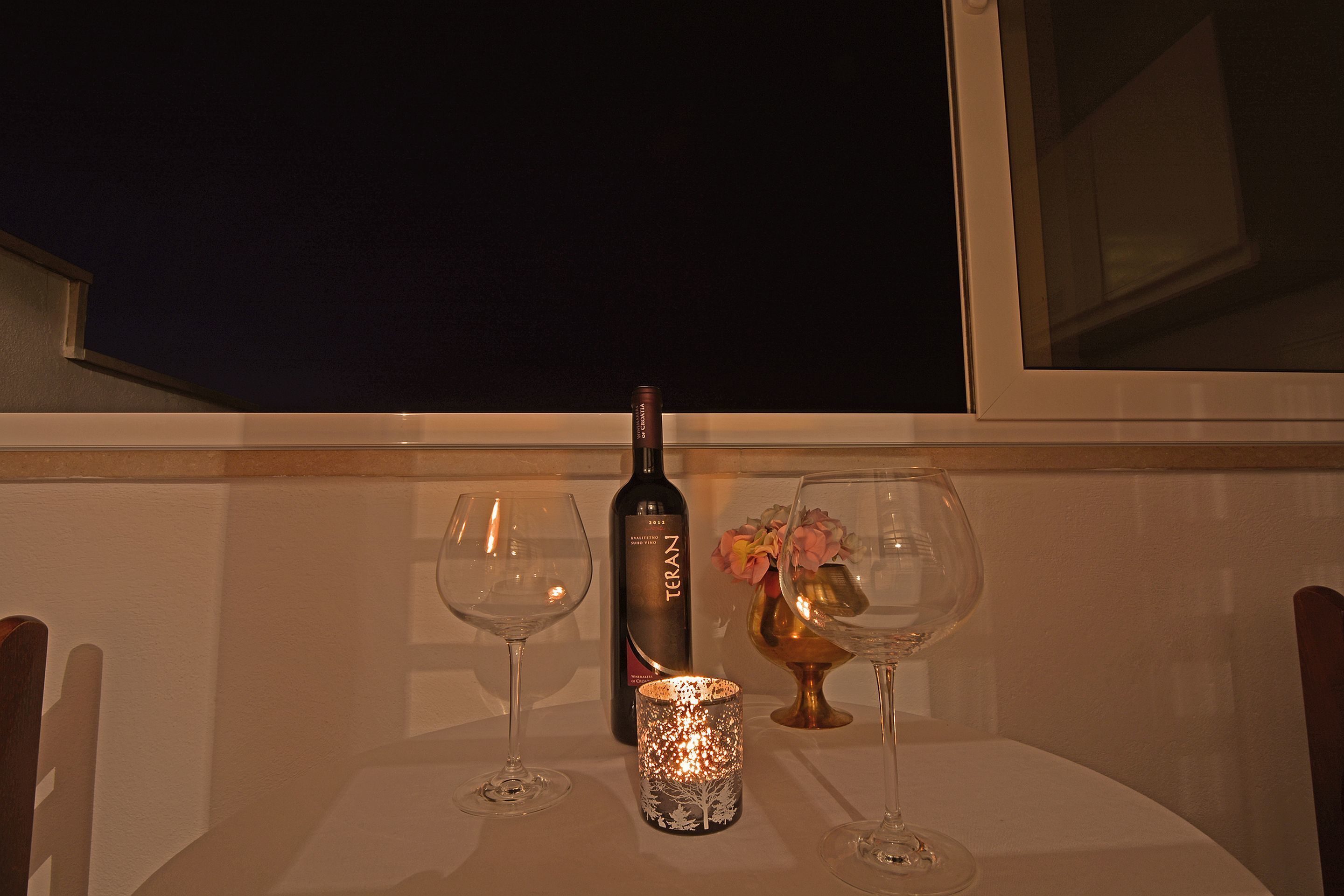 Uma mesa com uma garrafa de vinho, duas taças de vinho e uma vela acesa.