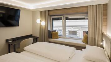 Quarto de hotel com duas camas, uma mesa de trabalho, uma televisão e janela com vista para a cidade.