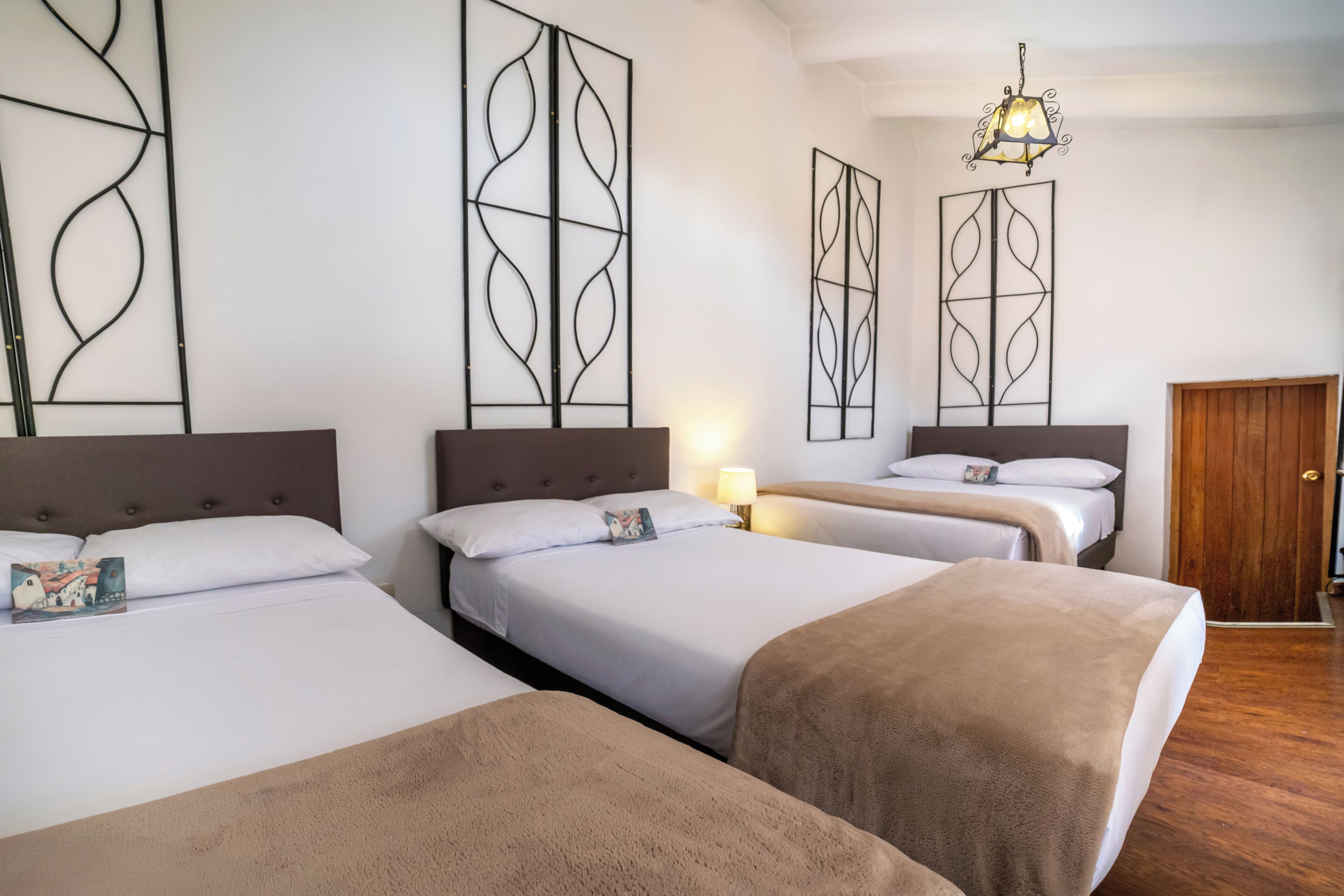 Quarto de hotel com três camas, cada uma com cabeceira, um guarda-roupa de madeira e painéis decorativos na parede.