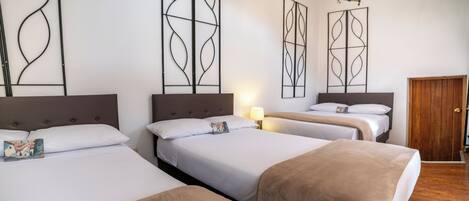Quarto de hotel com três camas, cada uma com cabeceira, um guarda-roupa de madeira e painéis decorativos na parede.