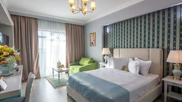 Quarto de hotel com uma cama grande, uma poltrona verde, uma escrivaninha com abajur e uma televisão.