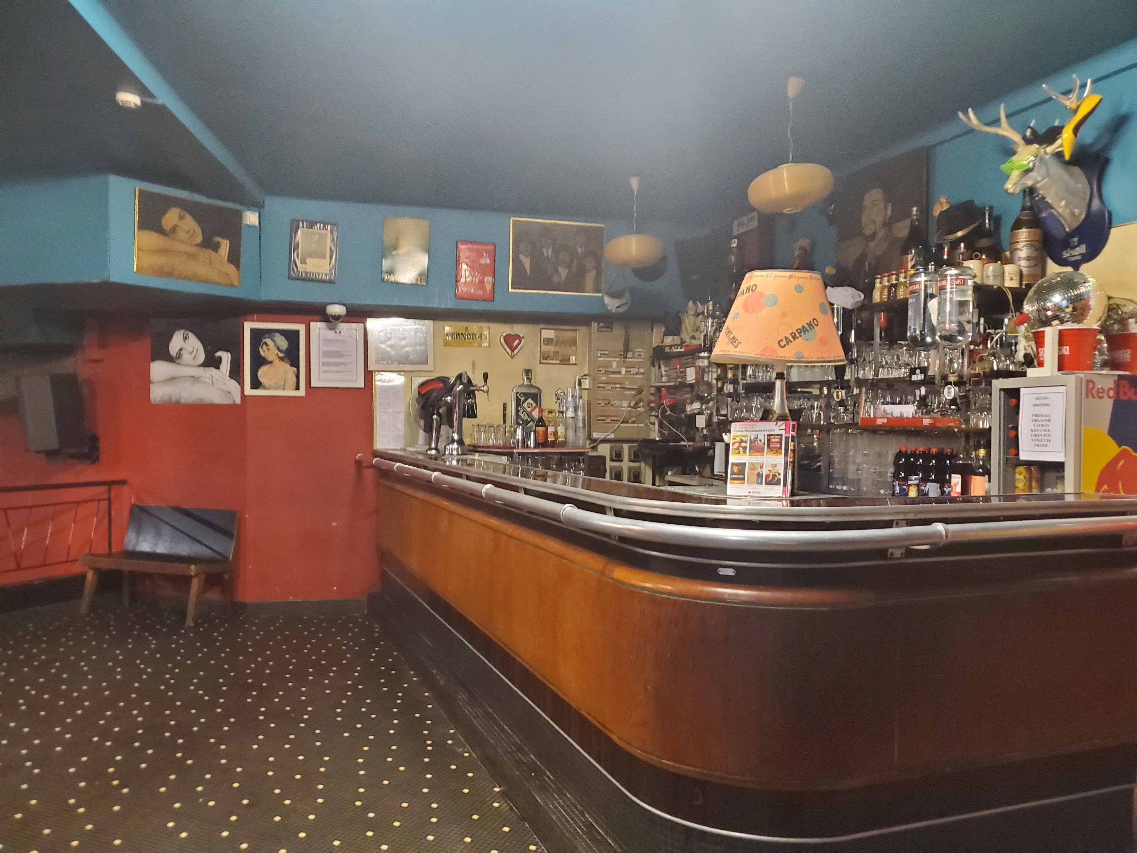 Uma área de bar com balcão, diversas garrafas e uma luminária.
