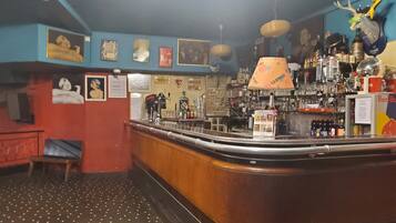 Uma área de bar com balcão, diversas garrafas e uma luminária.