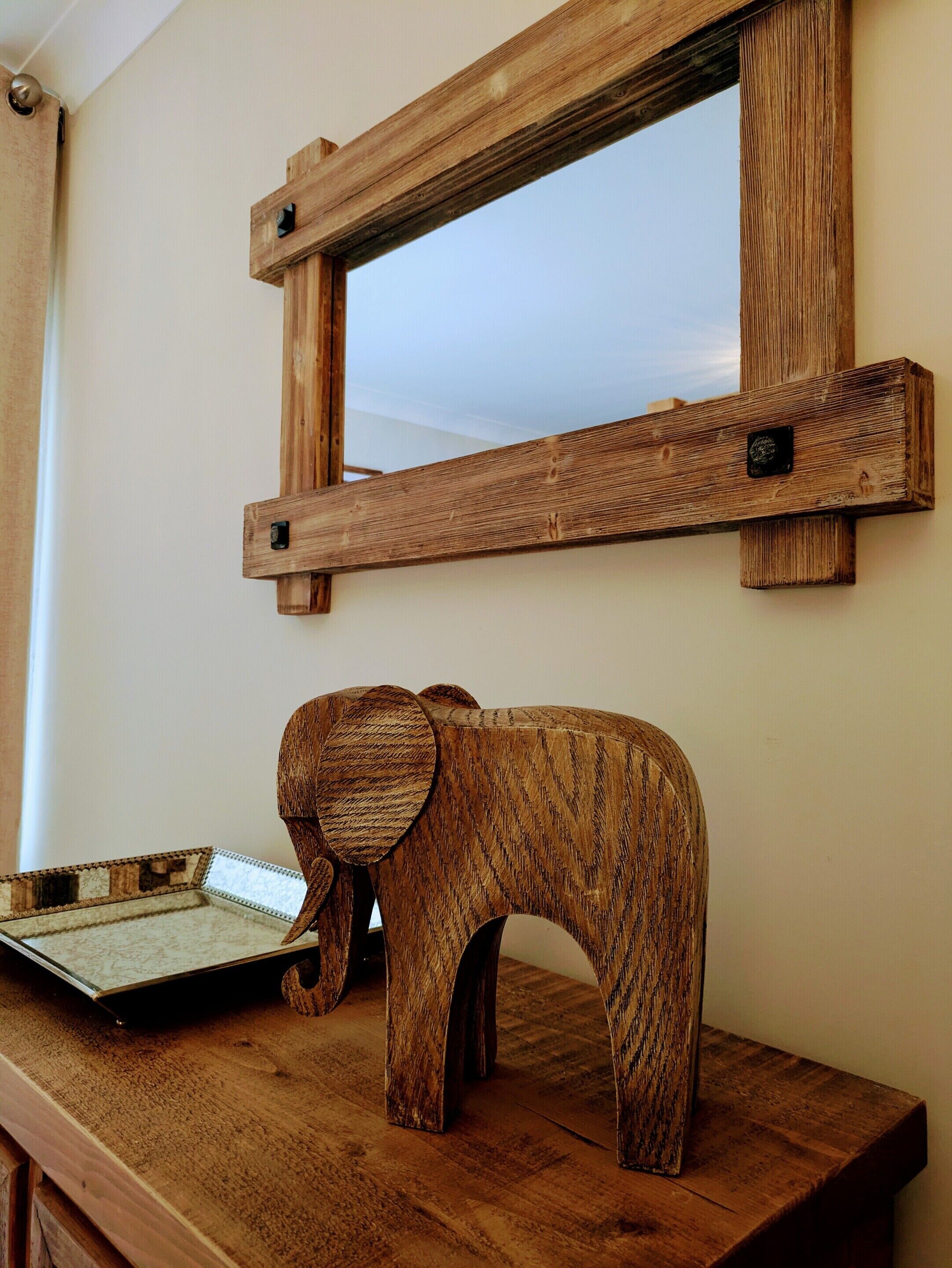 Uma escultura de elefante de madeira sobre uma mesa de madeira, com um espelho acima.