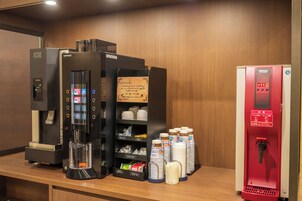 Uma estação de café com máquina de café, dispensador de bebidas e geladeira com visor digital.