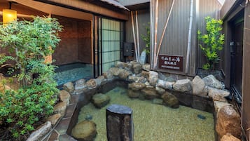 Área externa de águas termais com piscina de pedra, rodeada por rochas e vegetação.