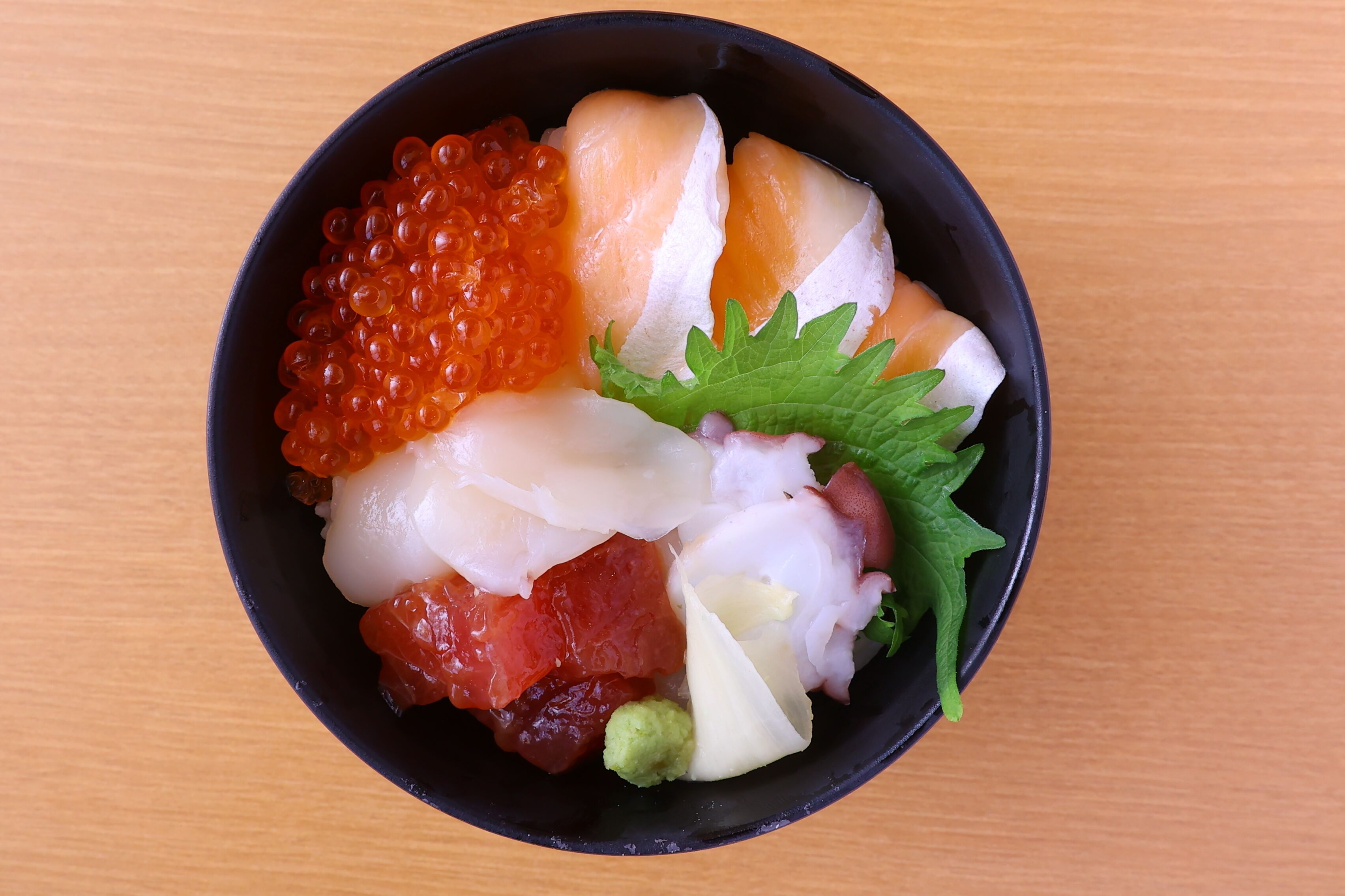 Uma tigela de sashimi com salmão, atum e ovas de salmão, decorada com uma folha.