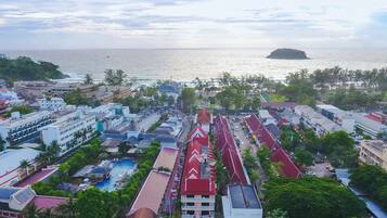 Vista aérea de uma cidade costeira com uma área de piscina em destaque, edifícios com telhados vermelhos e vista para o mar e uma ilha.
