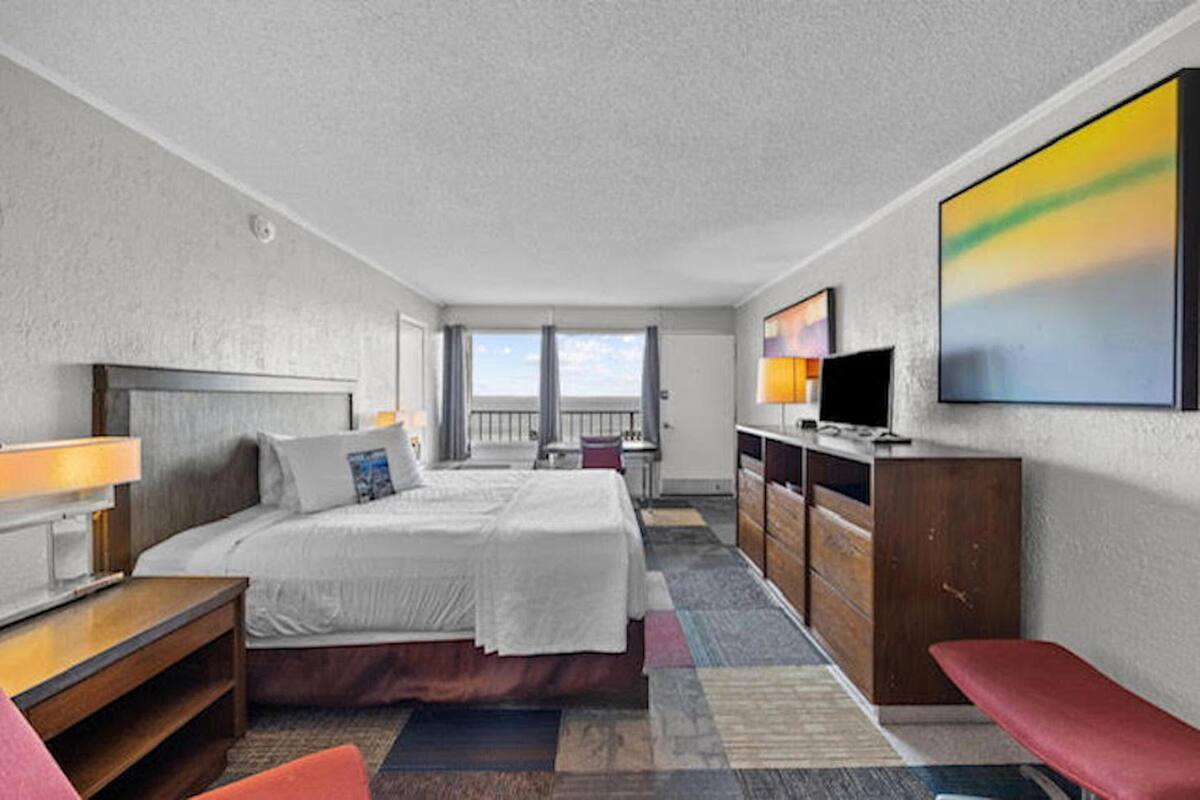 Quarto de hotel com uma cama grande, uma escrivaninha, uma televisão e uma varanda com vista.
