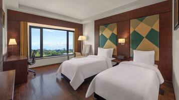 Quarto de hotel com duas camas, uma escrivaninha e uma cadeira. Uma janela grande oferece vista para o exterior.