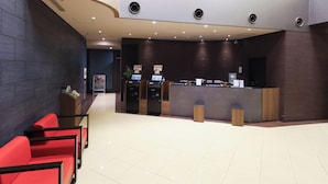 Um hall moderno com balcão de recepção, assentos vermelhos e teto alto com iluminação embutida.