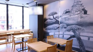Restaurante com mesas e cadeiras de madeira, uma janela grande e um mural na parede retratando um castelo tradicional japonês.