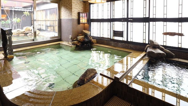 Uma onsen japonesa tradicional com interior de madeira, uma nascente quente de pedra e vista para o jardim exterior.