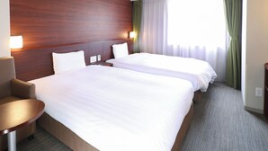 Quarto de hotel com duas camas, cabeceira de madeira, uma mesinha e uma janela com cortinas.