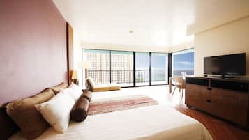 Quarto de hotel com uma cama grande, televisão, varanda com vista para edifícios e um armário de madeira.