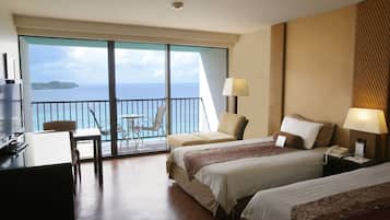 Quarto de hotel com duas camas, uma escrivaninha, cadeiras e vista para o mar.