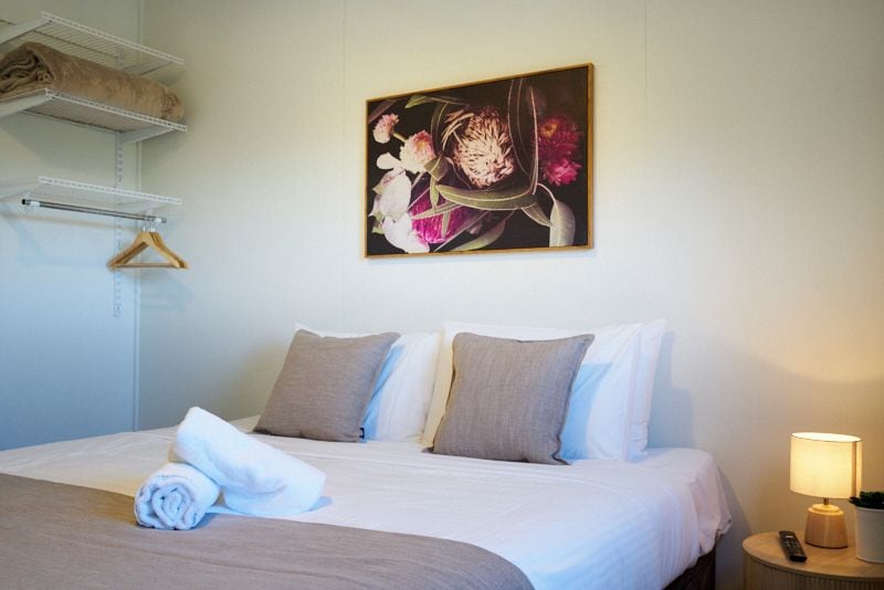 Cama bem arrumada com travesseiros, uma toalha enrolada e uma luminária de cabeceira.