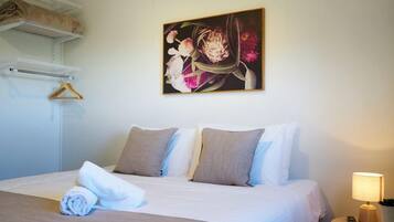 Cama bem arrumada com travesseiros, uma toalha enrolada e uma luminária de cabeceira.