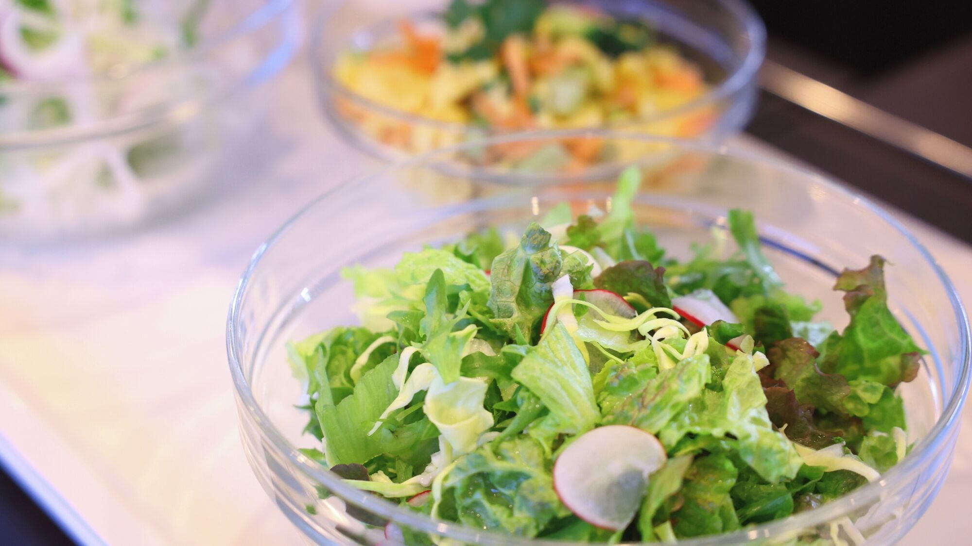 Uma tigela de vidro transparente cheia de salada, com alface, rabanetes e possivelmente outros vegetais.