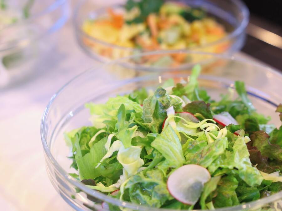 Uma tigela de vidro transparente cheia de salada, com alface, rabanetes e possivelmente outros vegetais.