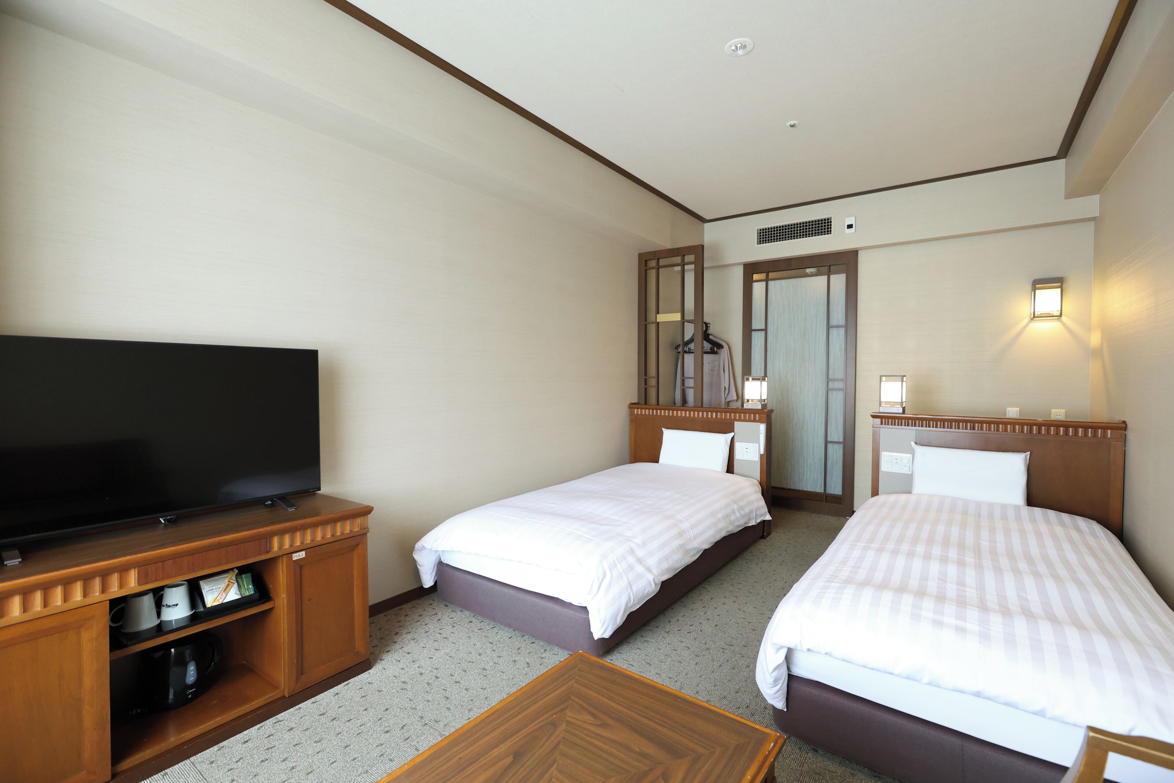 Quarto de hotel com duas camas, televisão, máquina de café e uma pequena mesa.
