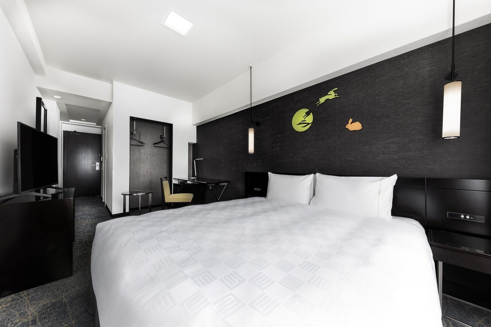 Quarto de hotel moderno com uma cama grande, uma escrivaninha, uma cadeira, uma televisão e um guarda-roupa.