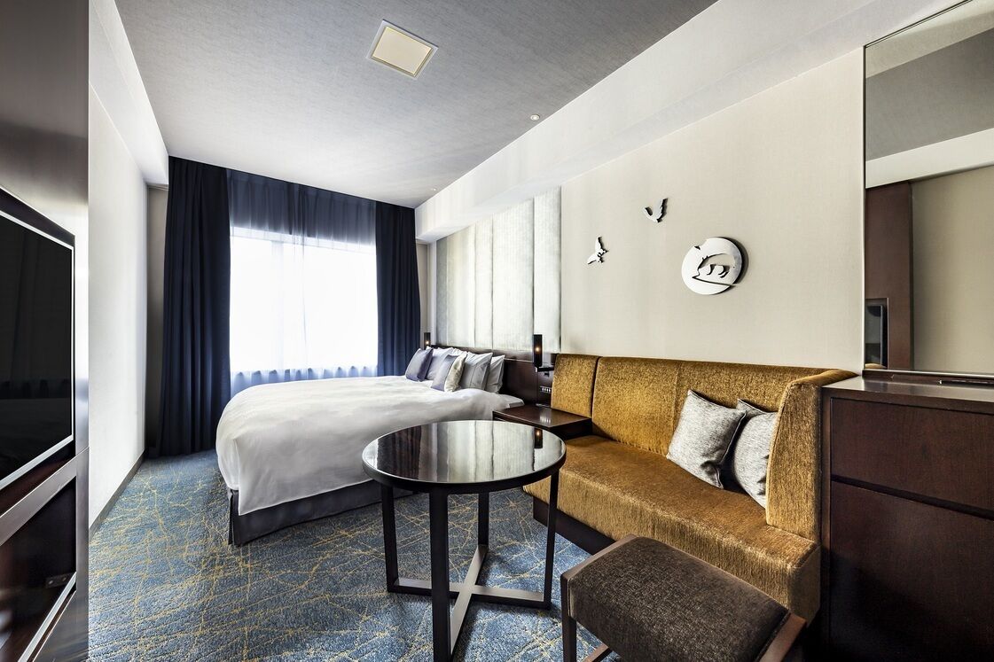 Quarto de hotel com cama, sofá, mesa redonda e televisão.