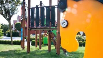 Um parquinho com uma estrutura de recreação em formato de cavalo amarelo e um escorrega de madeira ao fundo.