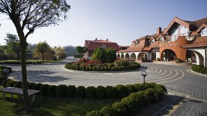 Um hotel com entrada circular, jardim ajardinado e prédio com telhado vermelho e janelas em arco.
