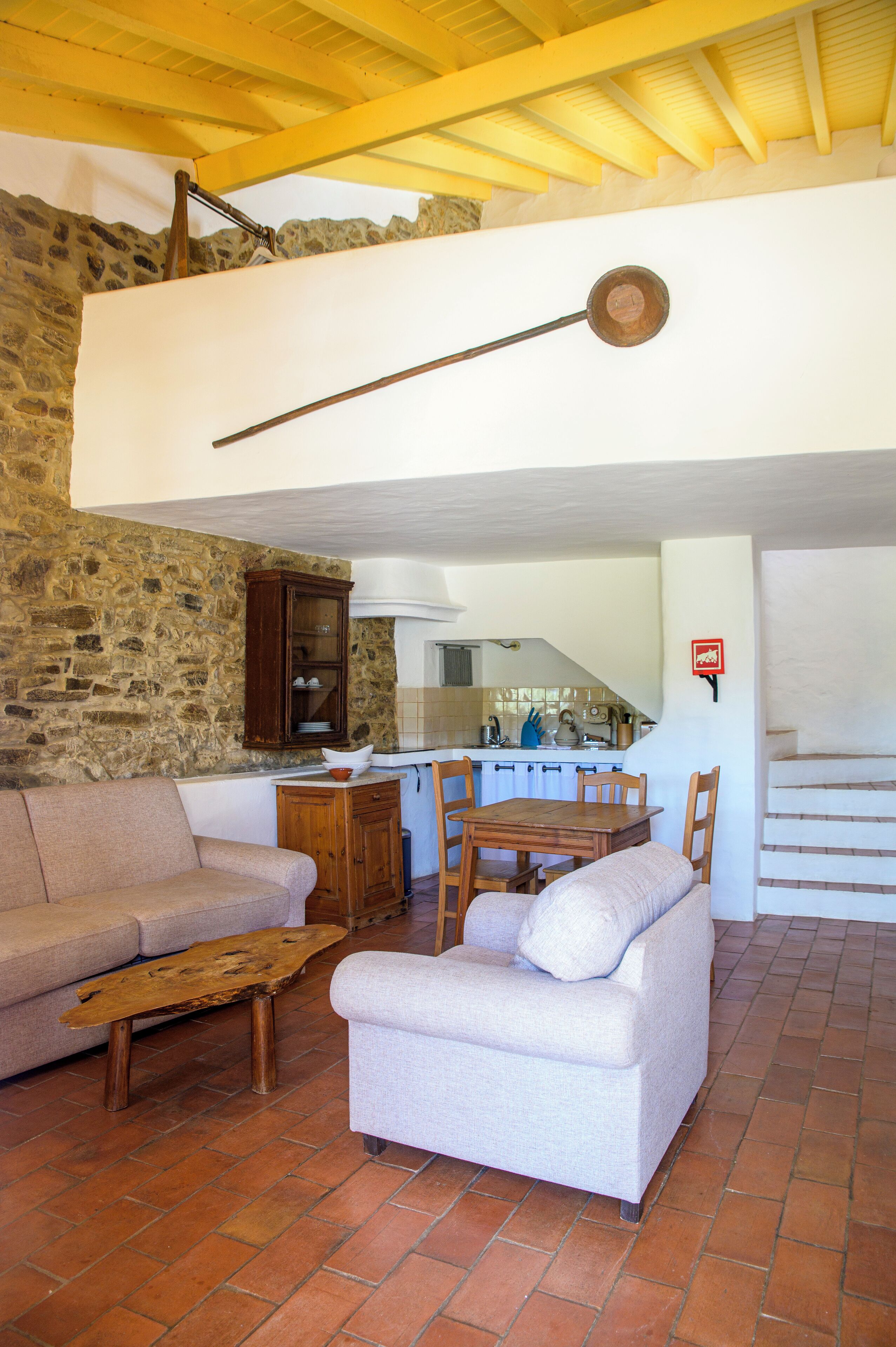 Uma sala de estar acolhedora com parede de pedra, uma mesa de jantar de madeira, um sofá e uma poltrona branca.