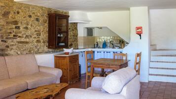 Uma sala de estar acolhedora com parede de pedra, uma mesa de jantar de madeira, um sofá e uma poltrona branca.
