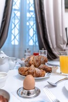 Uma mesa posta para o café da manhã com croissants, um copo de suco de laranja e uma chaleira.