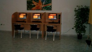 Quarto com escrivaninha de madeira, três monitores de computador, um vaso de planta e um quadro na parede.