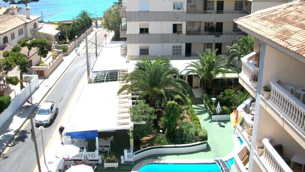 Um hotel com piscina, vista para o mar e uma rua com carros.