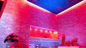 Um quarto de spa com parede de tijolos, mesa de massagem, decoração em formato de coração e um balão com a palavra 'love'.
