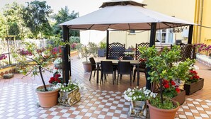 Um pátio externo com área de estar coberta, plantas em vasos e piso de azulejos.