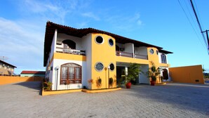 Um edifício de dois andares com fachada amarela, várias janelas e um pátio pavimentado.